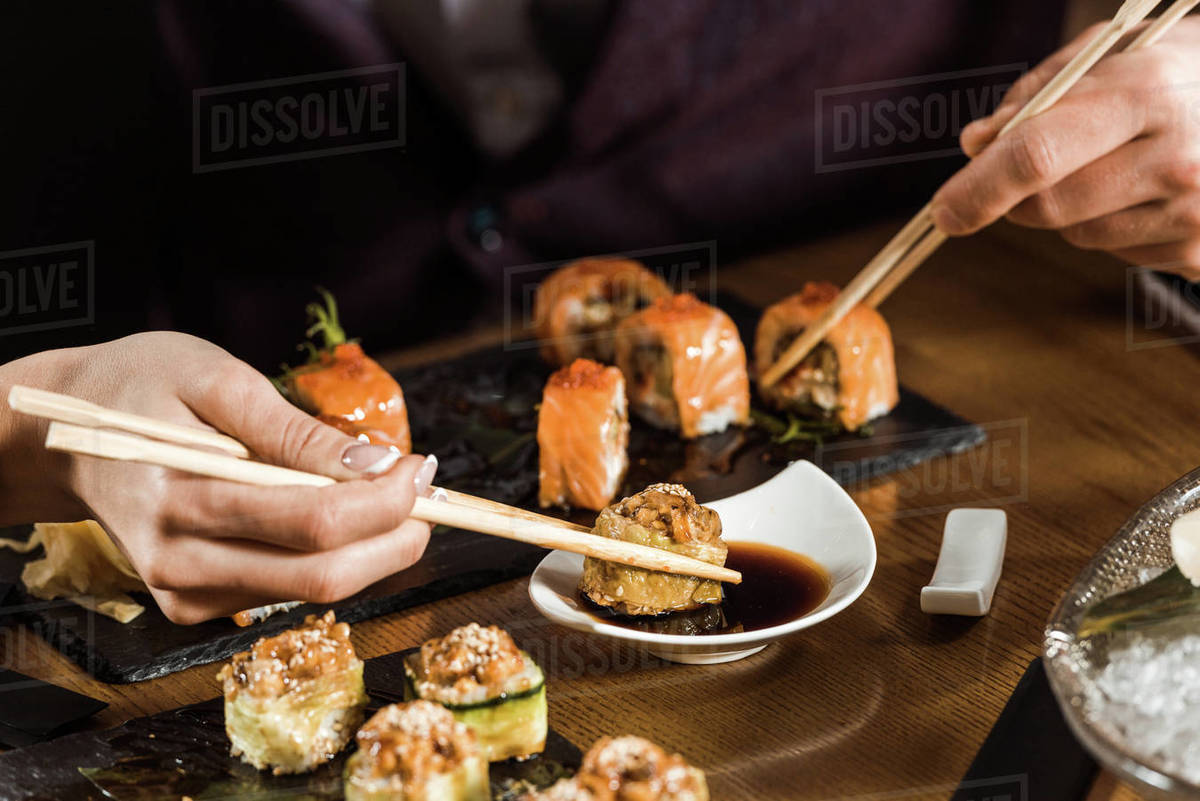 Cropped view of people eating sushi with chopsticks in restaurant ...
