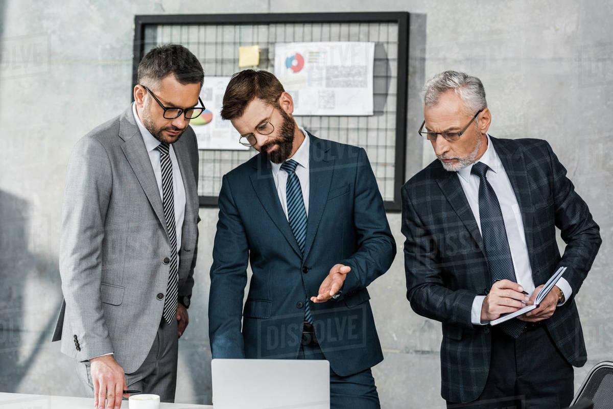 Three serious professional businessmen looking at laptop and discussing ...
