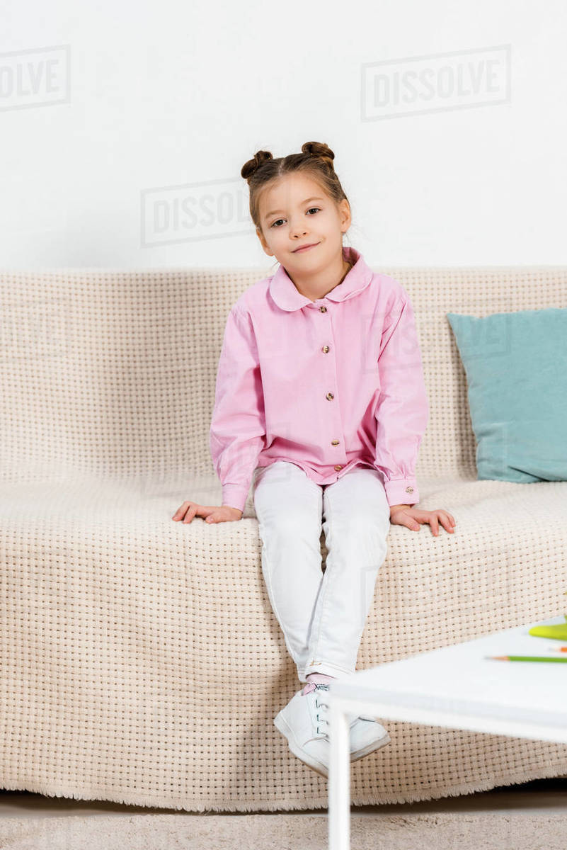 Full length view of adorable little kid sitting on couch and smiling at ...