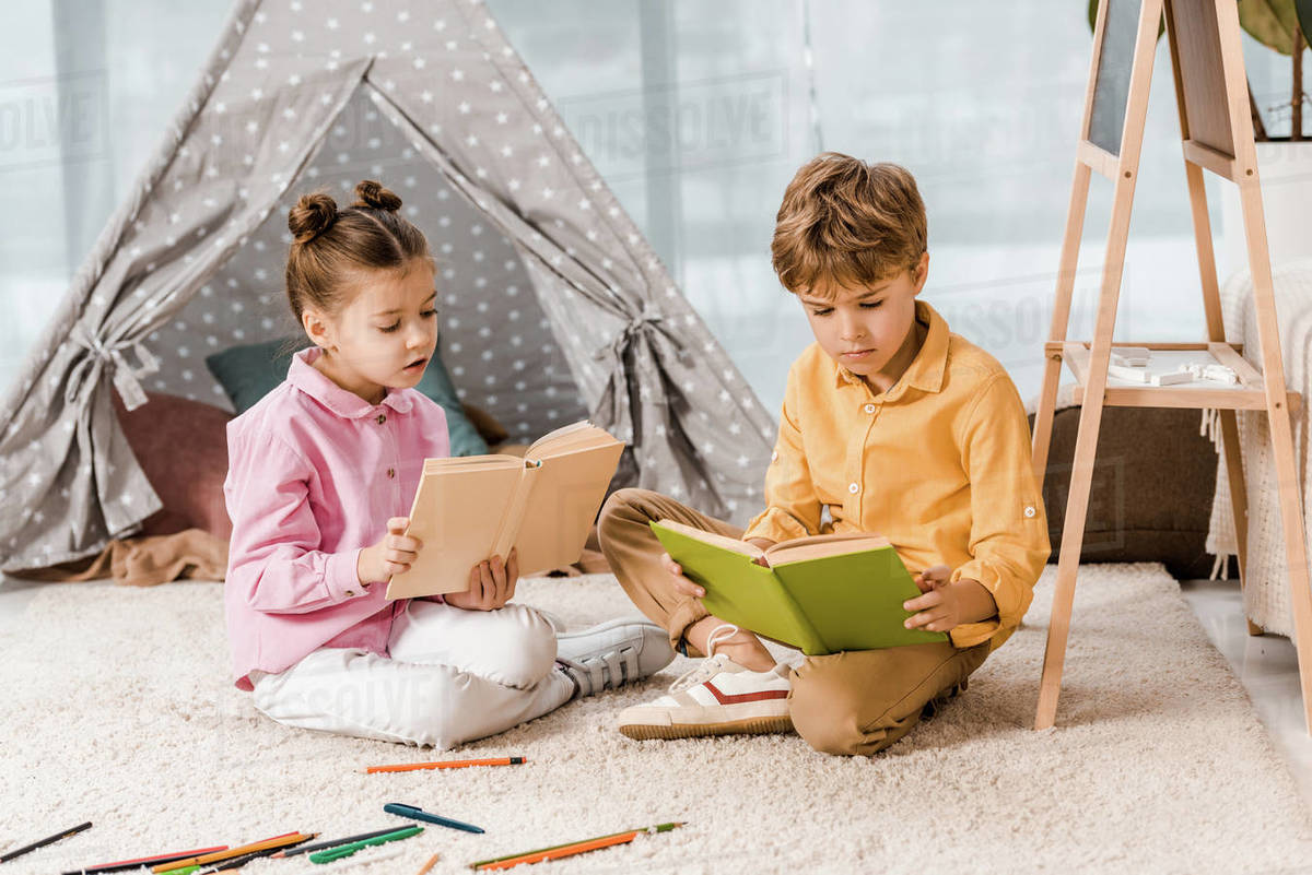 Beautiful focused children sitting on carpet and reading books together ...