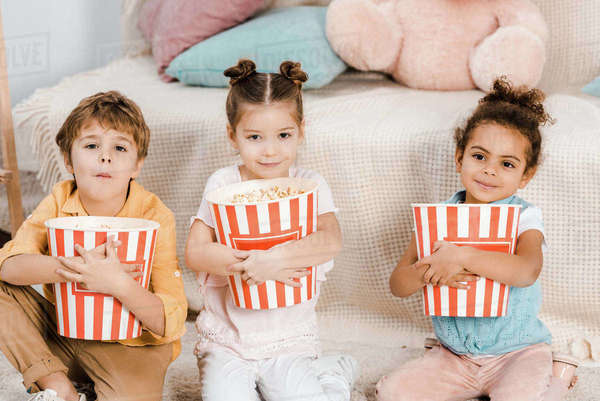 Adorable little kids holding boxes with popcorn and smiling at camera ...