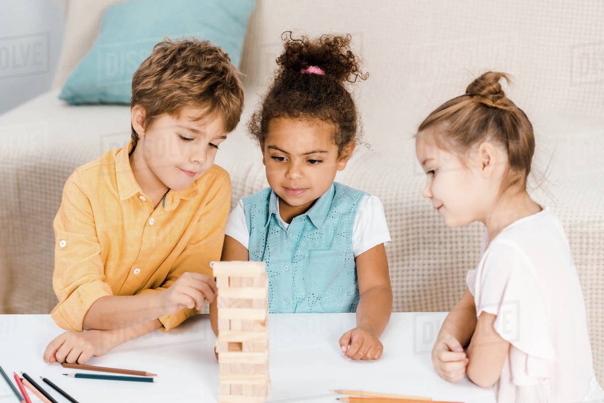 Cute happy children building tower from wooden blocks on table ...