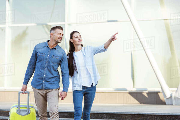 A couple of tourists looking away, smiling and pointing at something ...