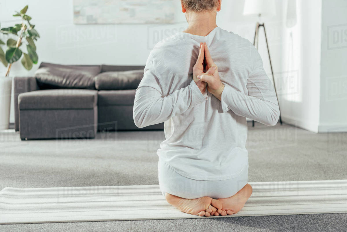Cropped shot of man sitting in yoga pose with hands behind back at home ...