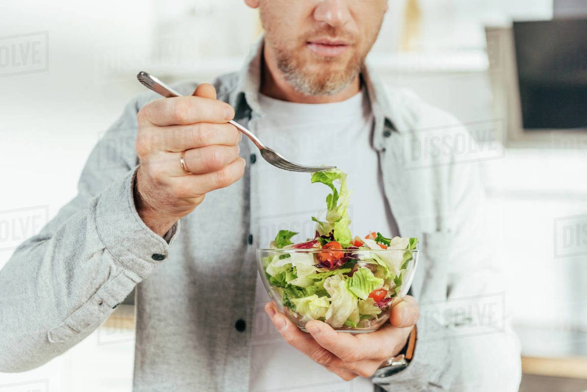 Cropped shot of man eating vegetable salad at home - Stock Photo - Dissolve