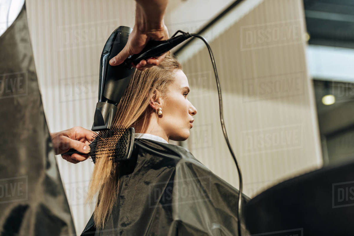 low angle view of hairdresser drying hair to attractive girl in beauty ...