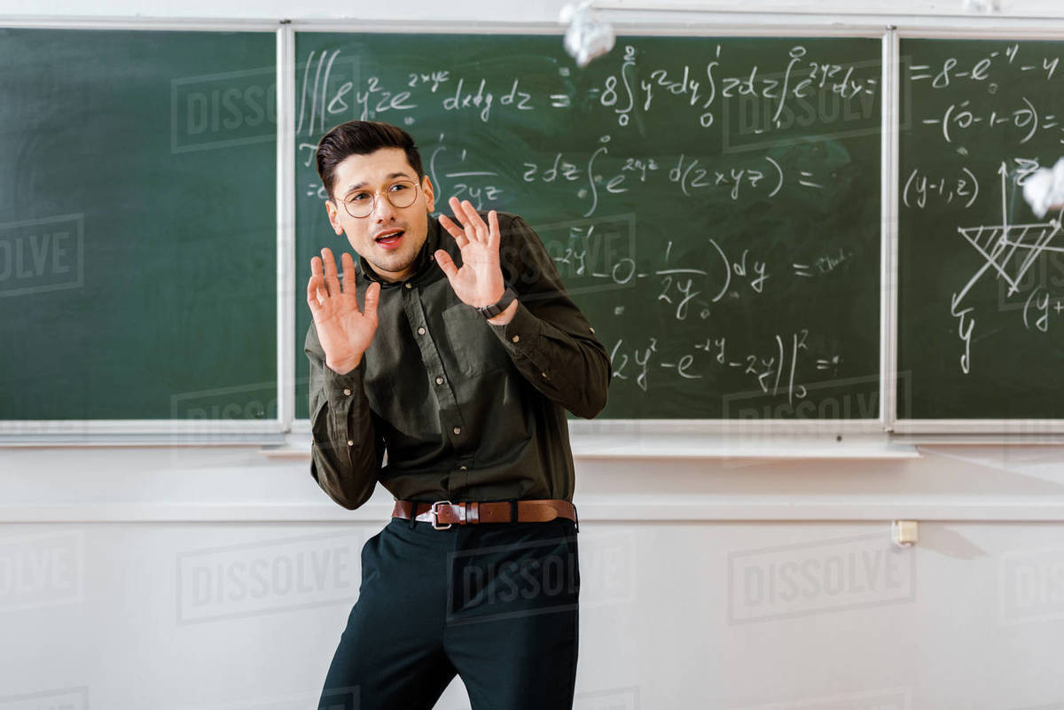 Crumpled paper balls flying at frightened male teacher in classroom ...