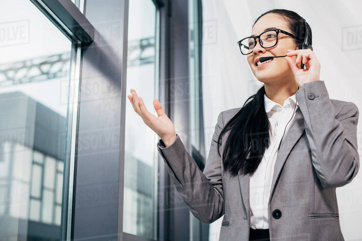 Attractive call center operator standing by window and speaking in ...