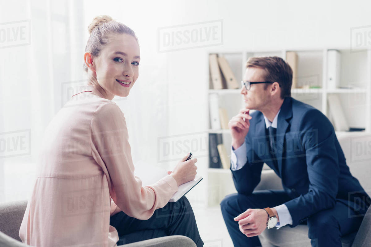 Cheerful journalist taking notes during interview with businessman in ...