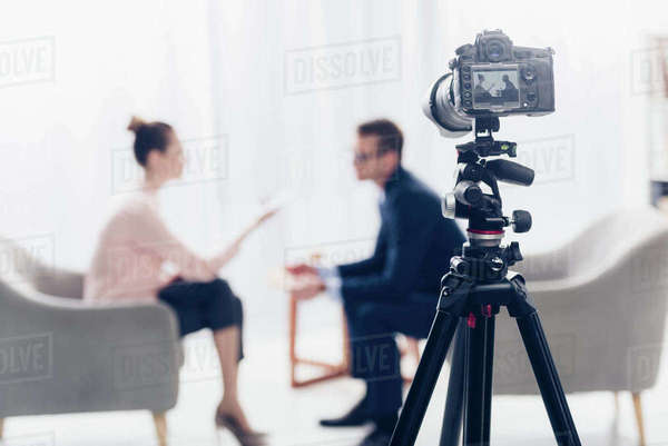 Businessman giving interview to journalist in office, camera on tripod ...