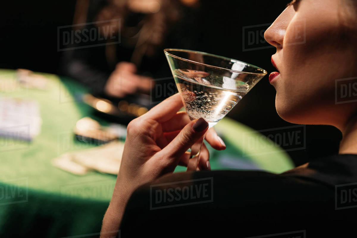 Cropped image of girl drinking cocktail while playing poker at table in ...