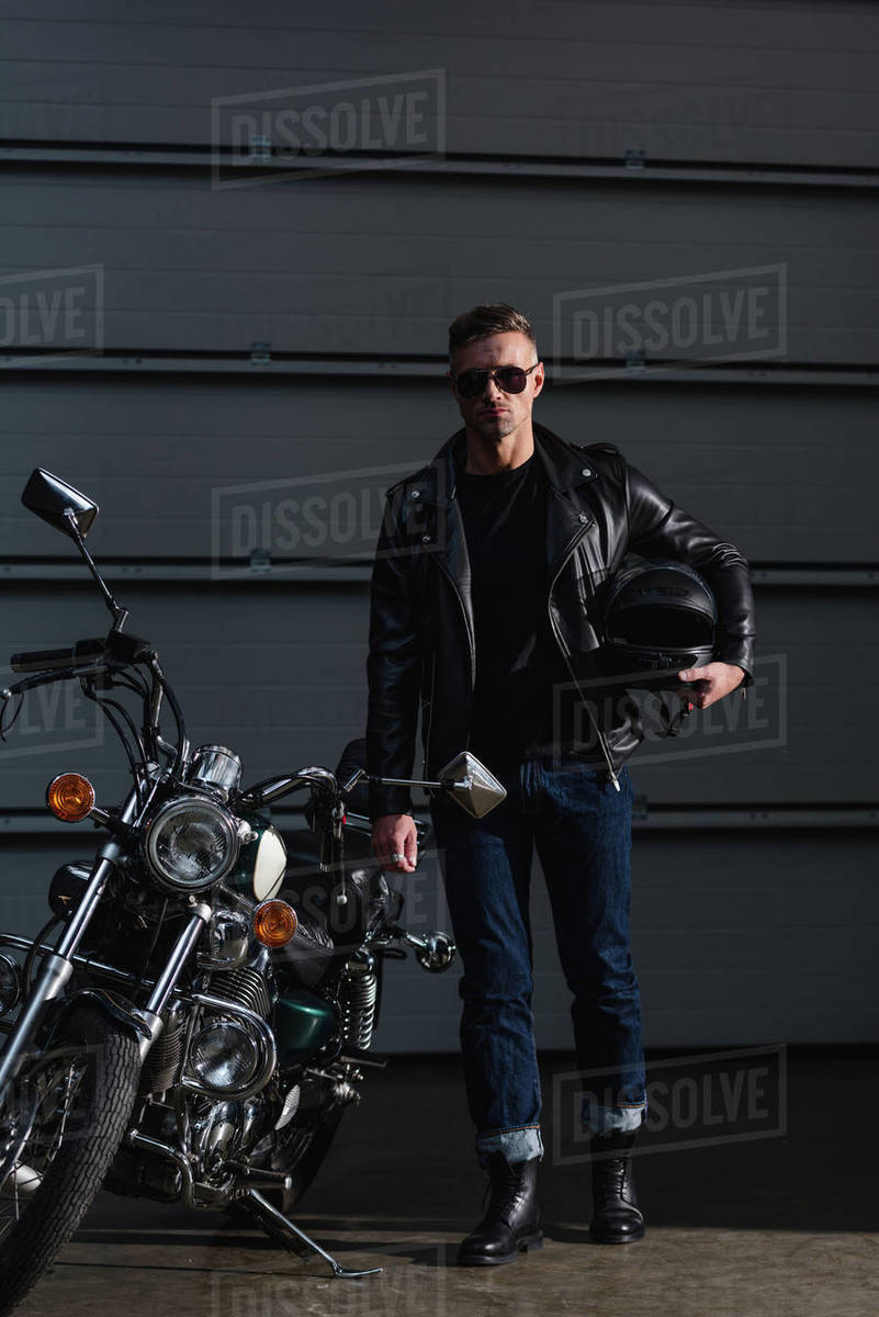 Stylish biker in black sunglasses and leather jacket standing by ...