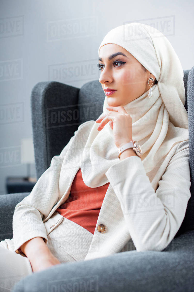 Beautiful pensive young muslim woman sitting in chair and looking away ...