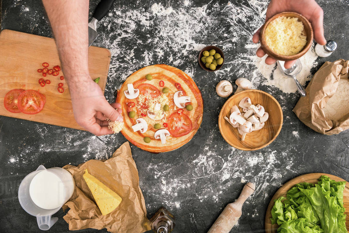 Cropped view of man putting ingredients on pizza on grey background ...
