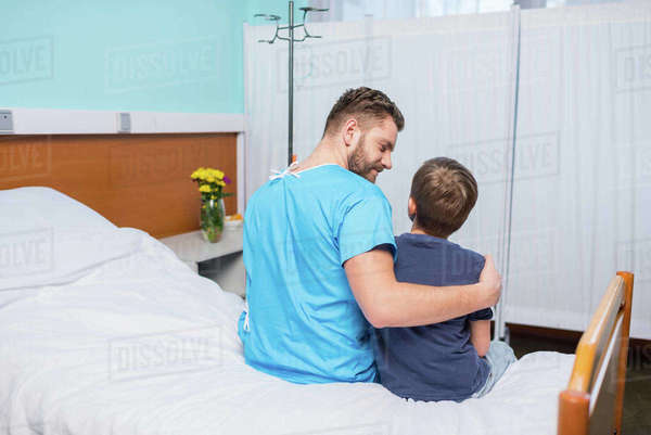 Back view of smiling father and little son sitting together on hospital ...