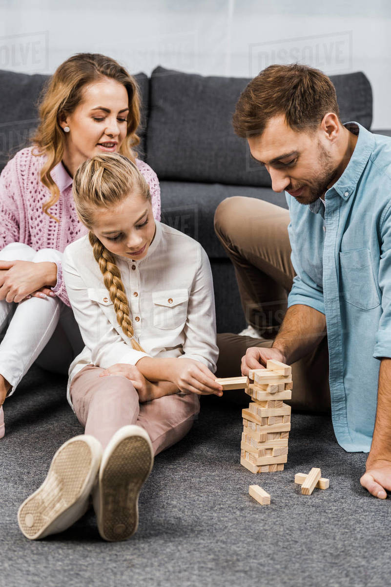 Two happy parents playing blocks wood tower game with daughter on floor ...