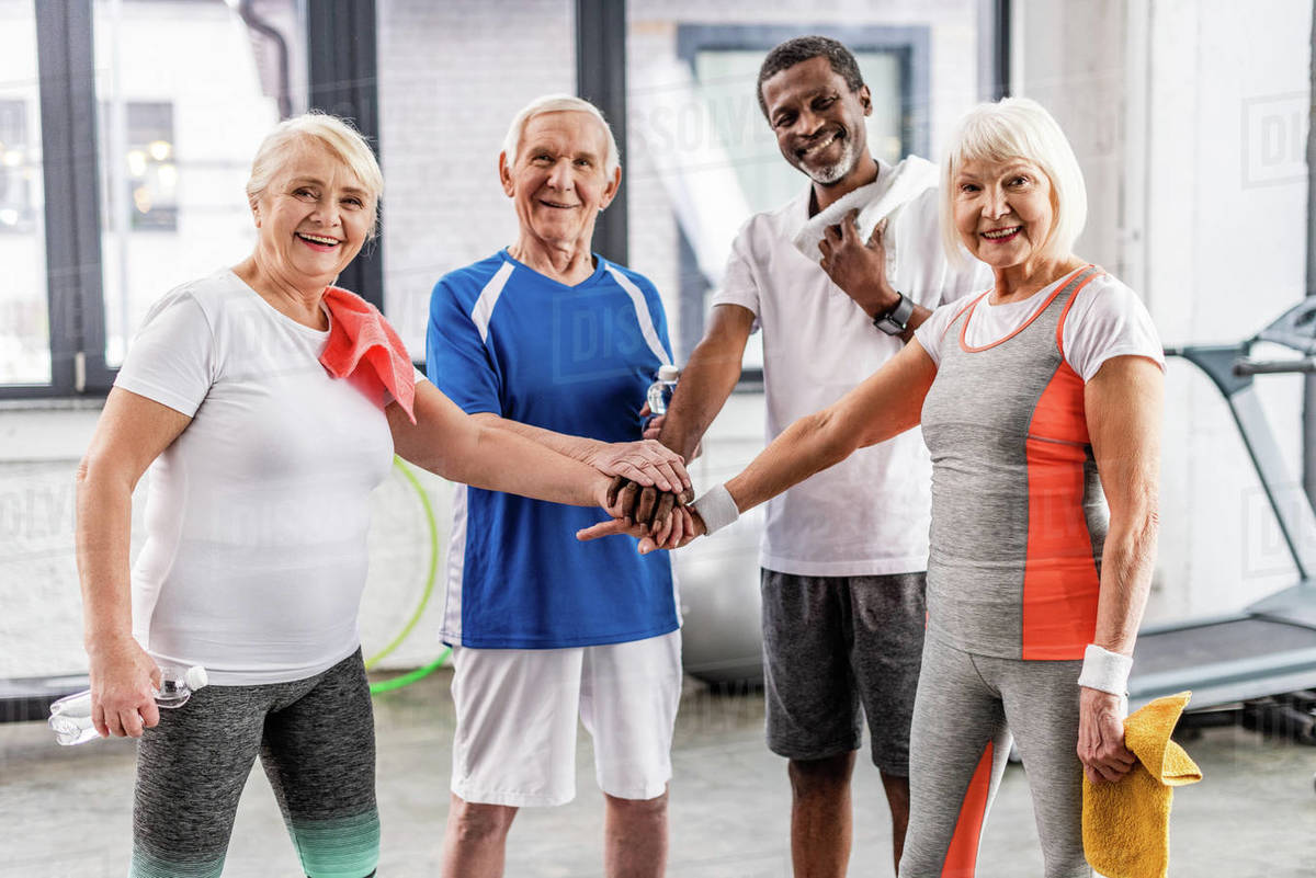 Happy senior multicultural friends putting hands together at sports ...