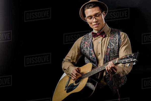 Handsome male musician in eyeglasses and hat playing on acoustic guitar ...