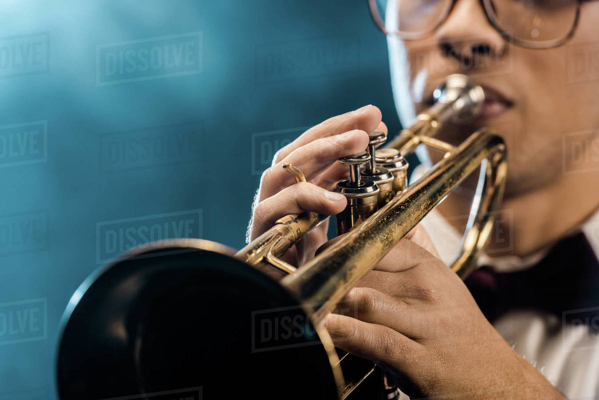 Cropped shot of male musician playing on trumpet on stage with dramatic ...