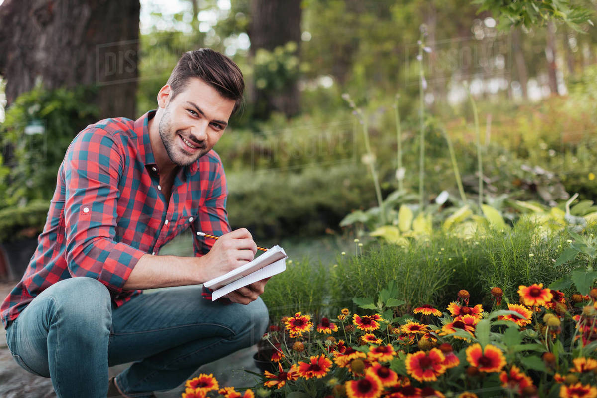 Smiling gardener with notebook in hands looking at camera in garden ...