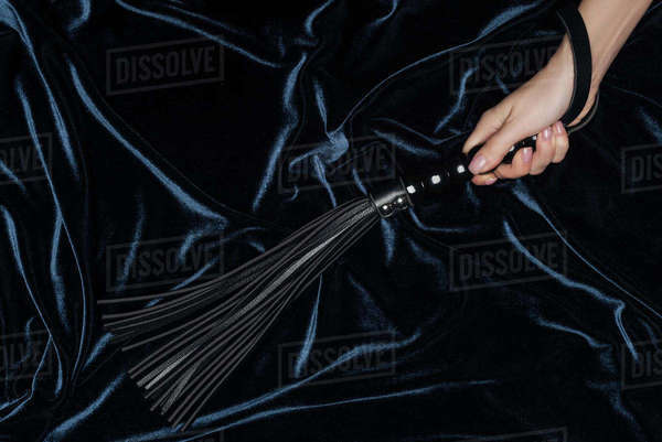 Close up of female hand holding flogging whip with dark velvet cloth at ...