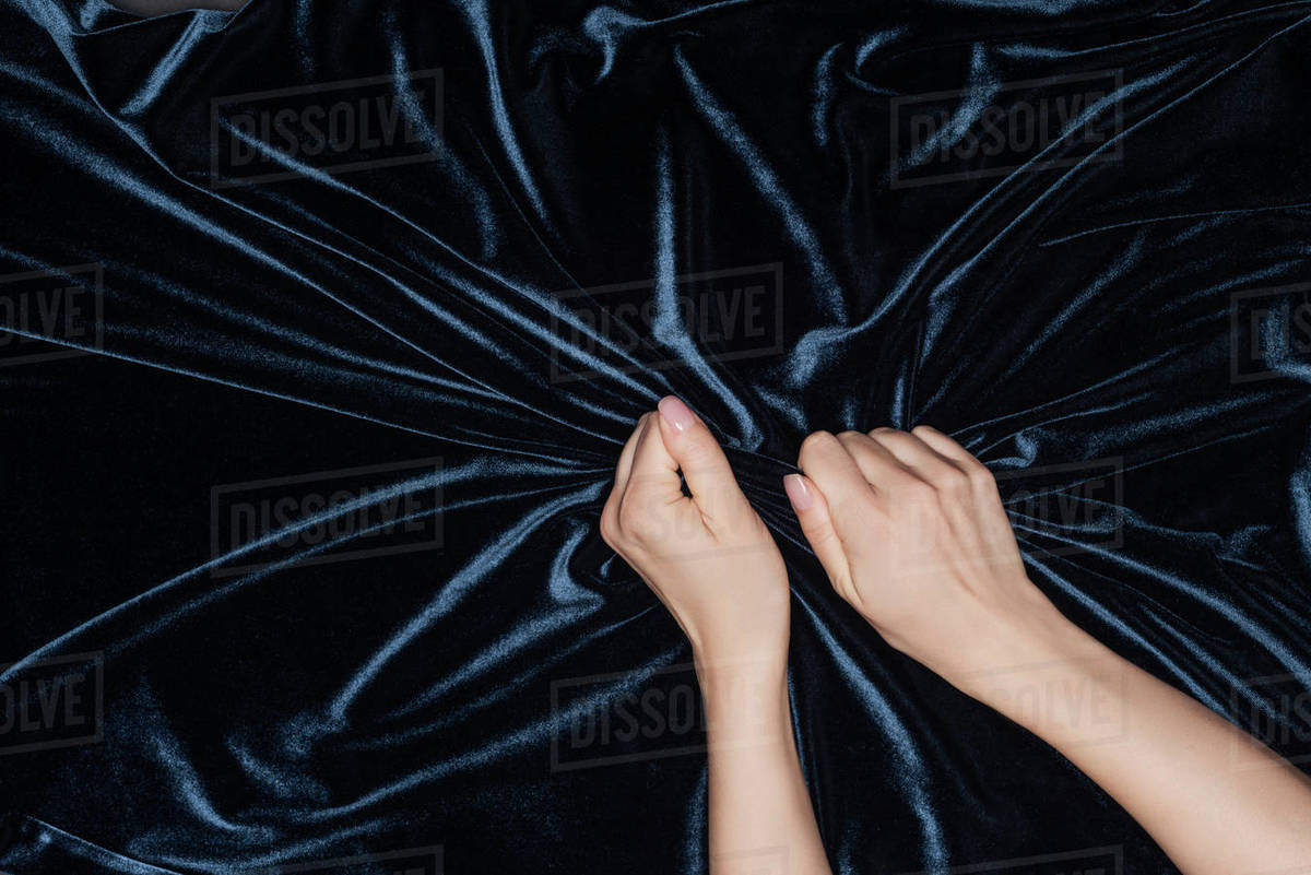 Close up of female hands tightly holding black shiny velvet cloth ...