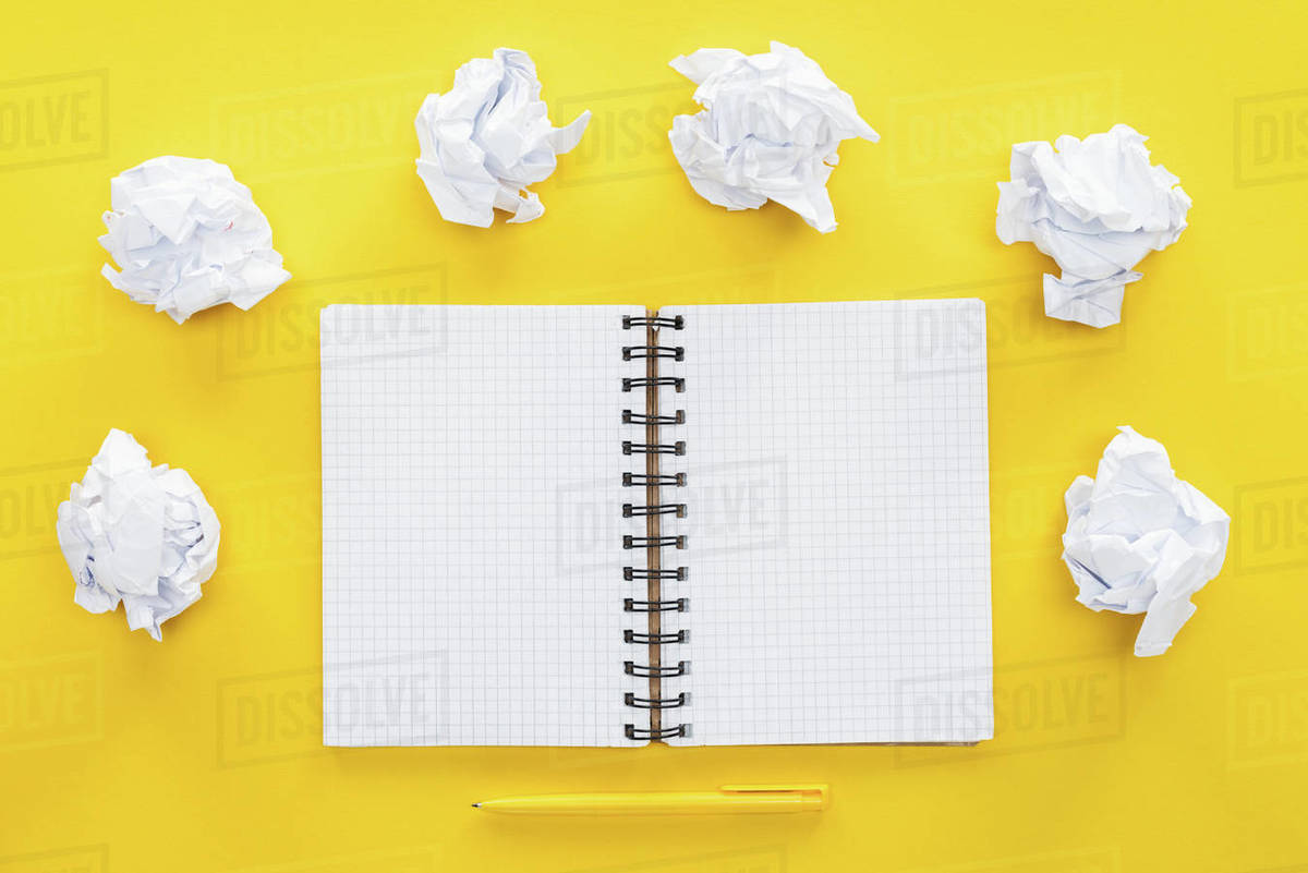 Blank spiral notebook and crumbled paper balls on yellow background ...