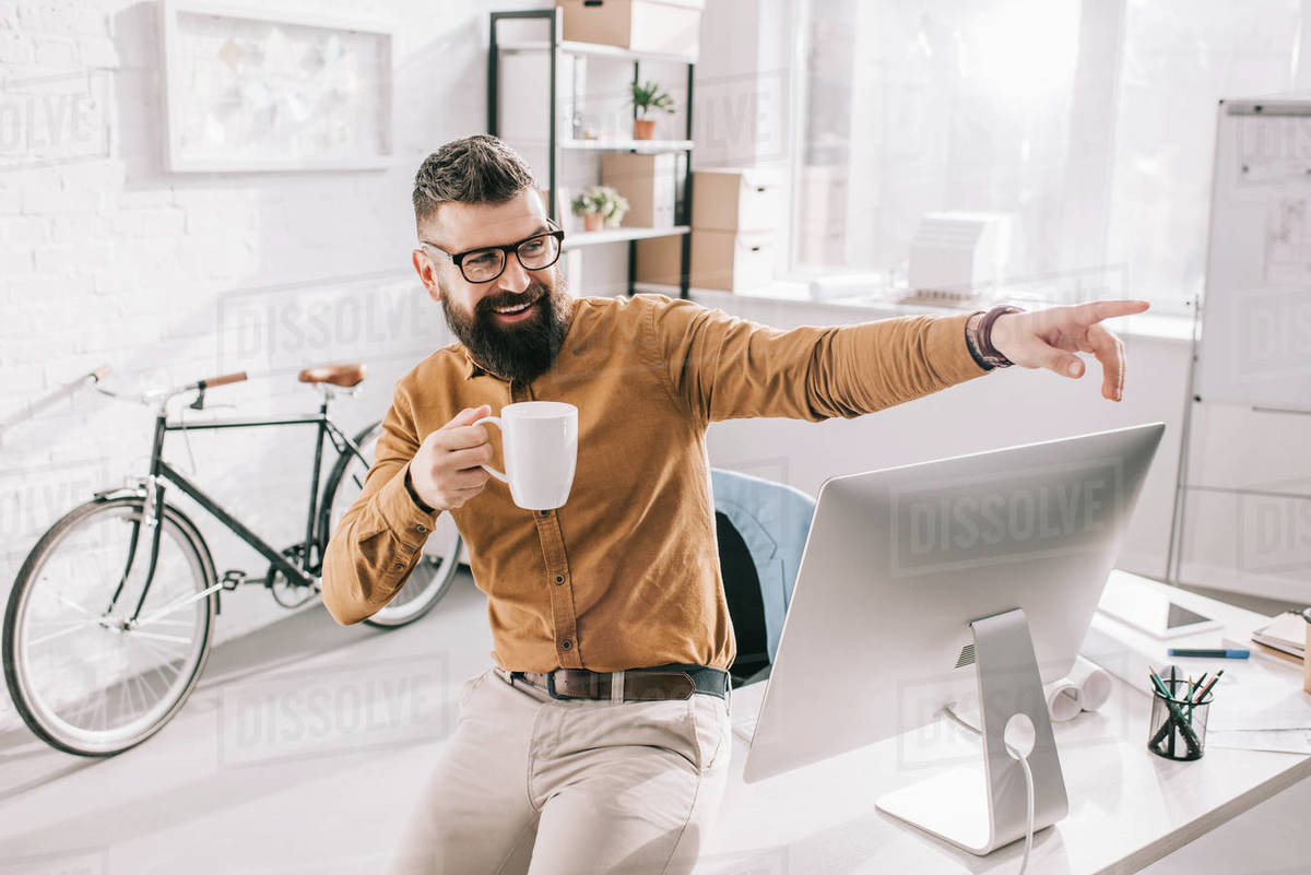 Happy bearded adult businessman holding cup of coffee and pointing ...