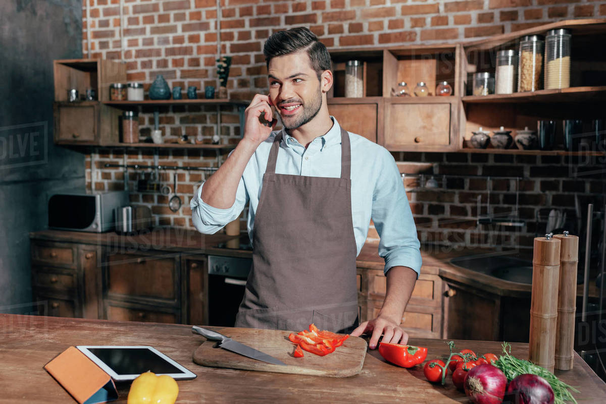 Handsome young man cooking and talking by phone - Stock Photo - Dissolve