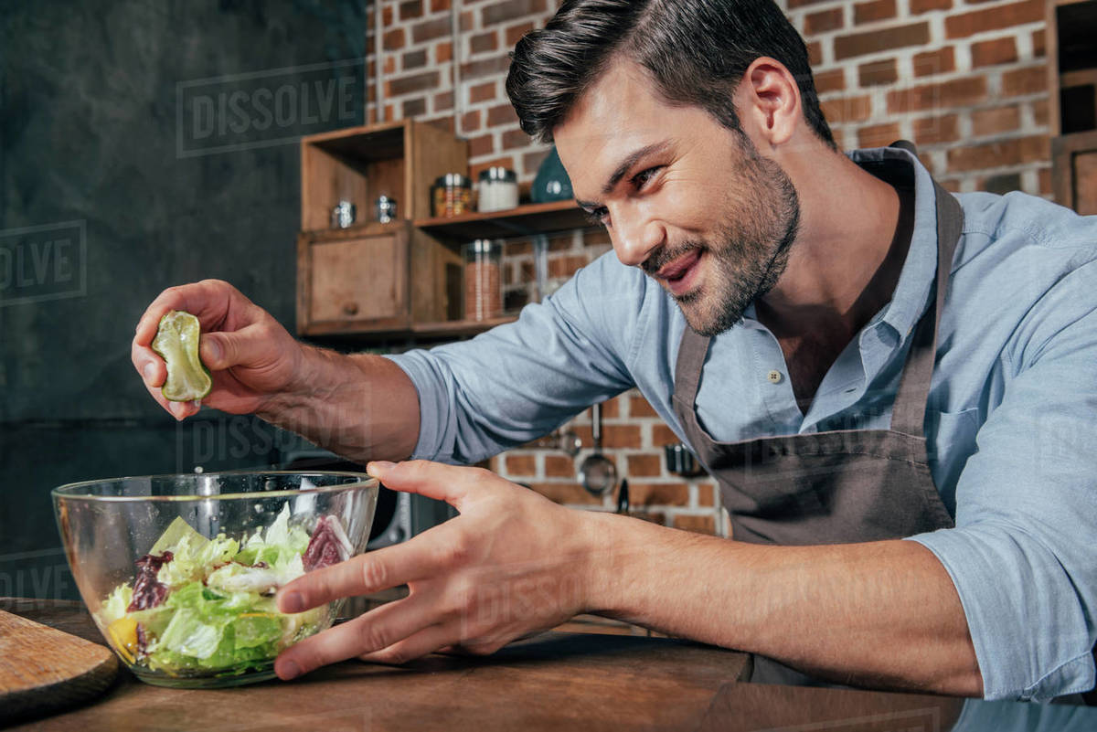 Excited young man making salad - Royalty-free Stock Photo | Dissolve