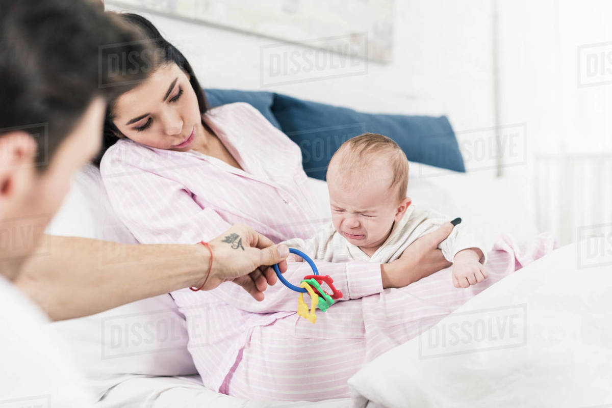 Mother holding crying baby in hands with father near by at home ...