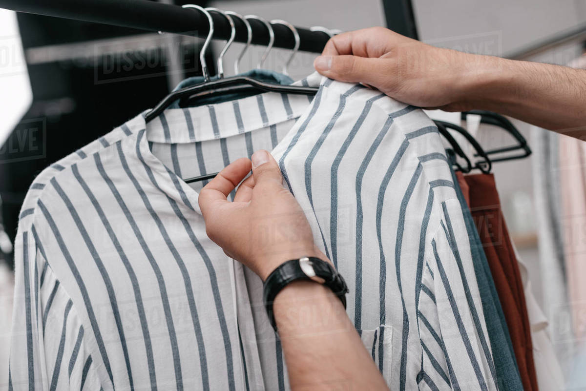 Close-up partial view of young man working with clothes on hangers in ...