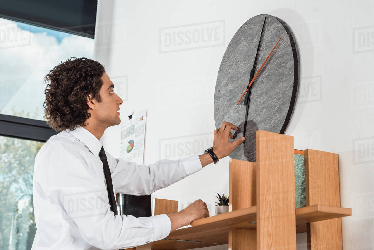 Side view of young businessman setting time on clock in office ...