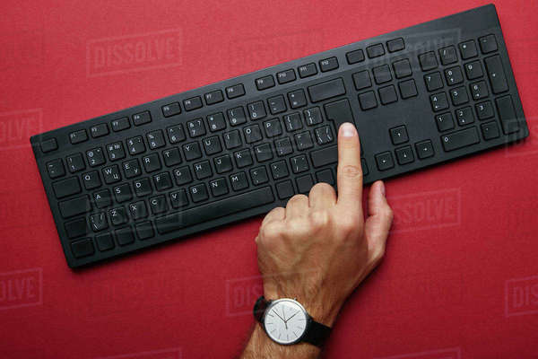 Top view of male hand pushing button on black computer keyboard on red ...