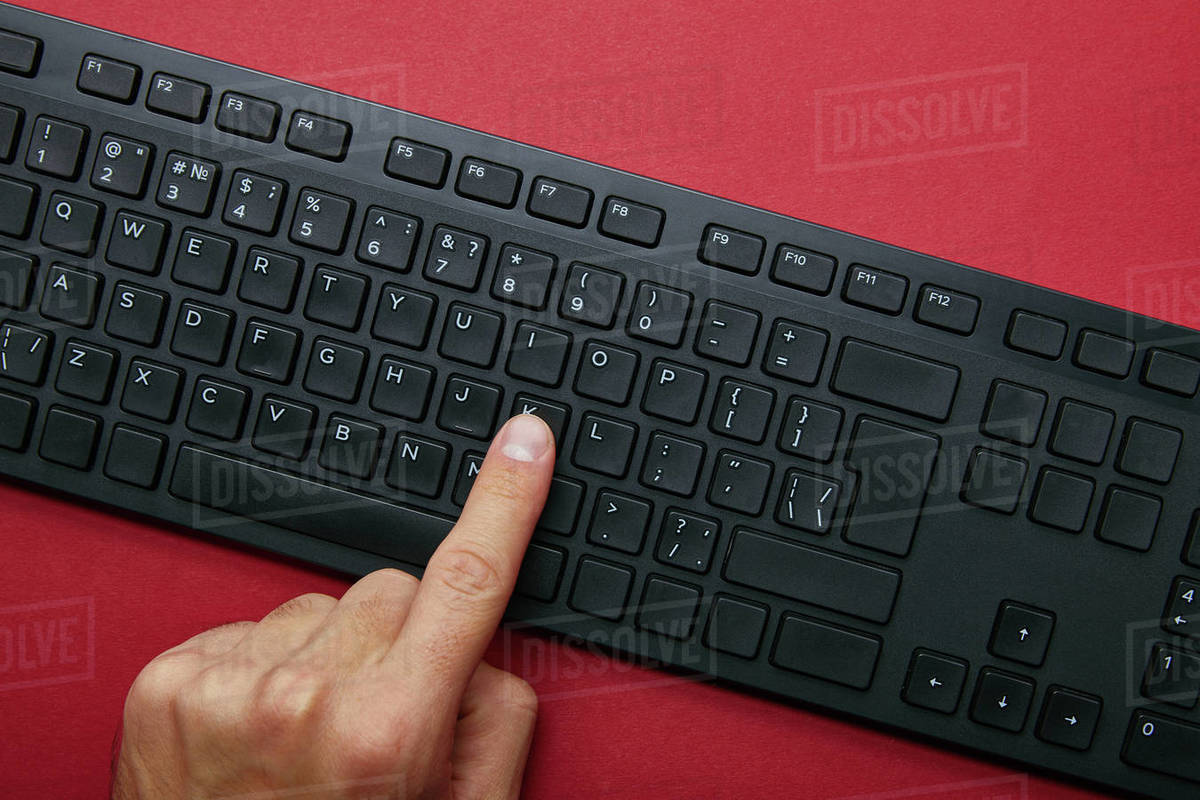 Cropped view of man pushing button on black computer keyboard on red ...