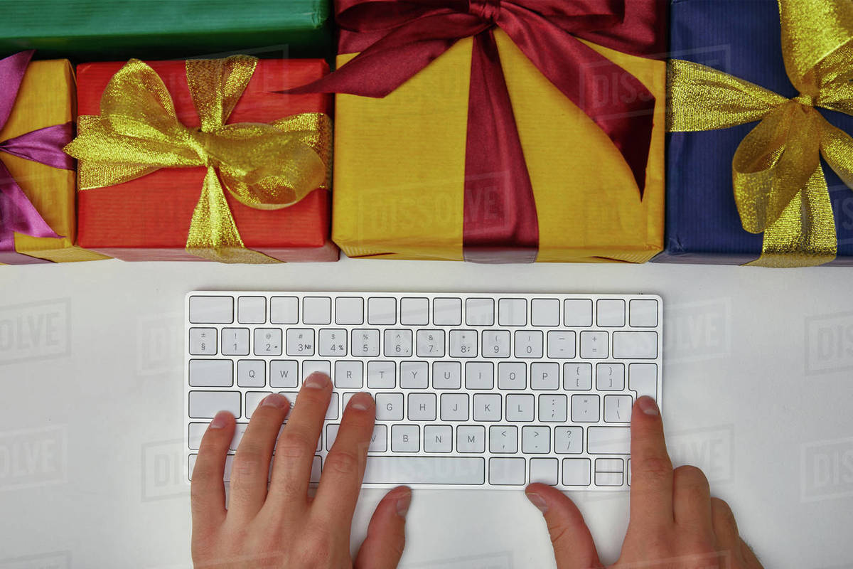 Top view of man typing on computer keyboard near wrapped gifts on white ...
