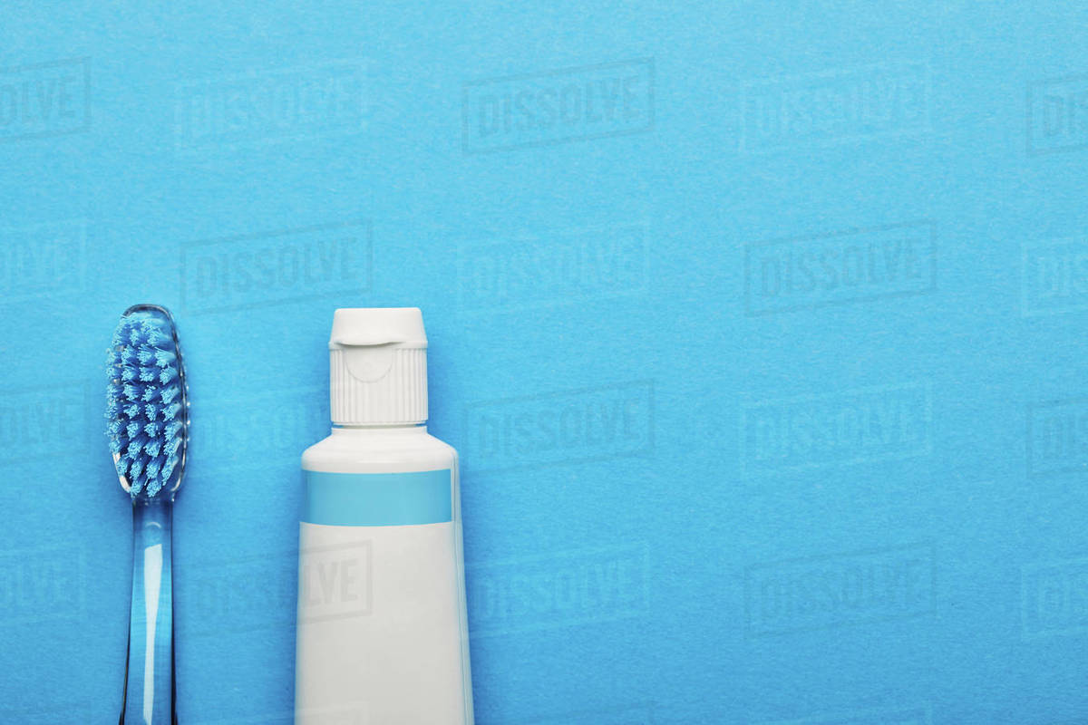 Top view of toothbrush and toothpaste arranged on blue backdrop ...