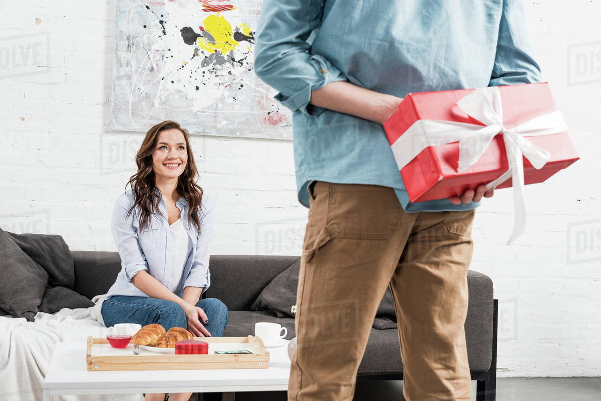 Back view of man holding red birthday present behind back with smiling ...