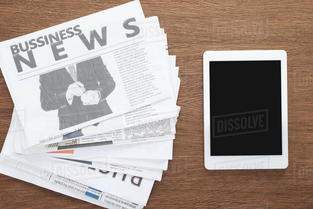 Top view of tablet with blank screen and business newspapers on wooden ...