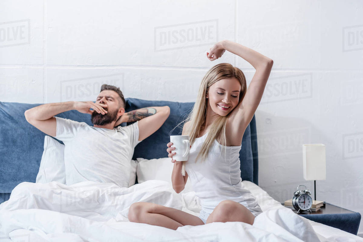 Bearded man yawning while attractive young woman with coffee cup ...