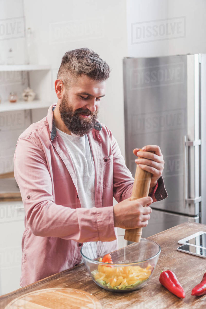 Handsome smiling man salting salad in bowl at kitchen table - Royalty ...