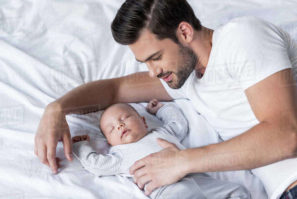 Handsome father lying on bed with sleeping baby boy - Royalty-free ...