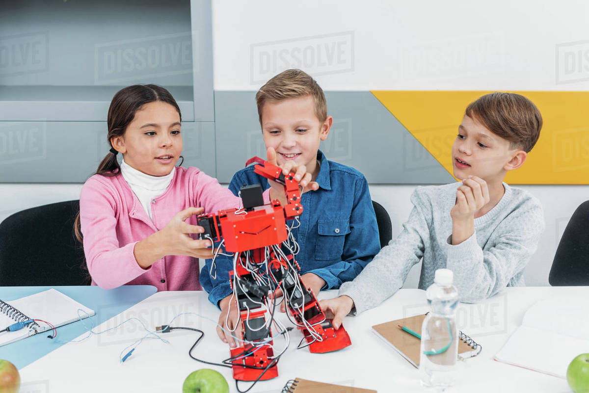 Smiling schoolchildren building red electric robot during stem lesson ...