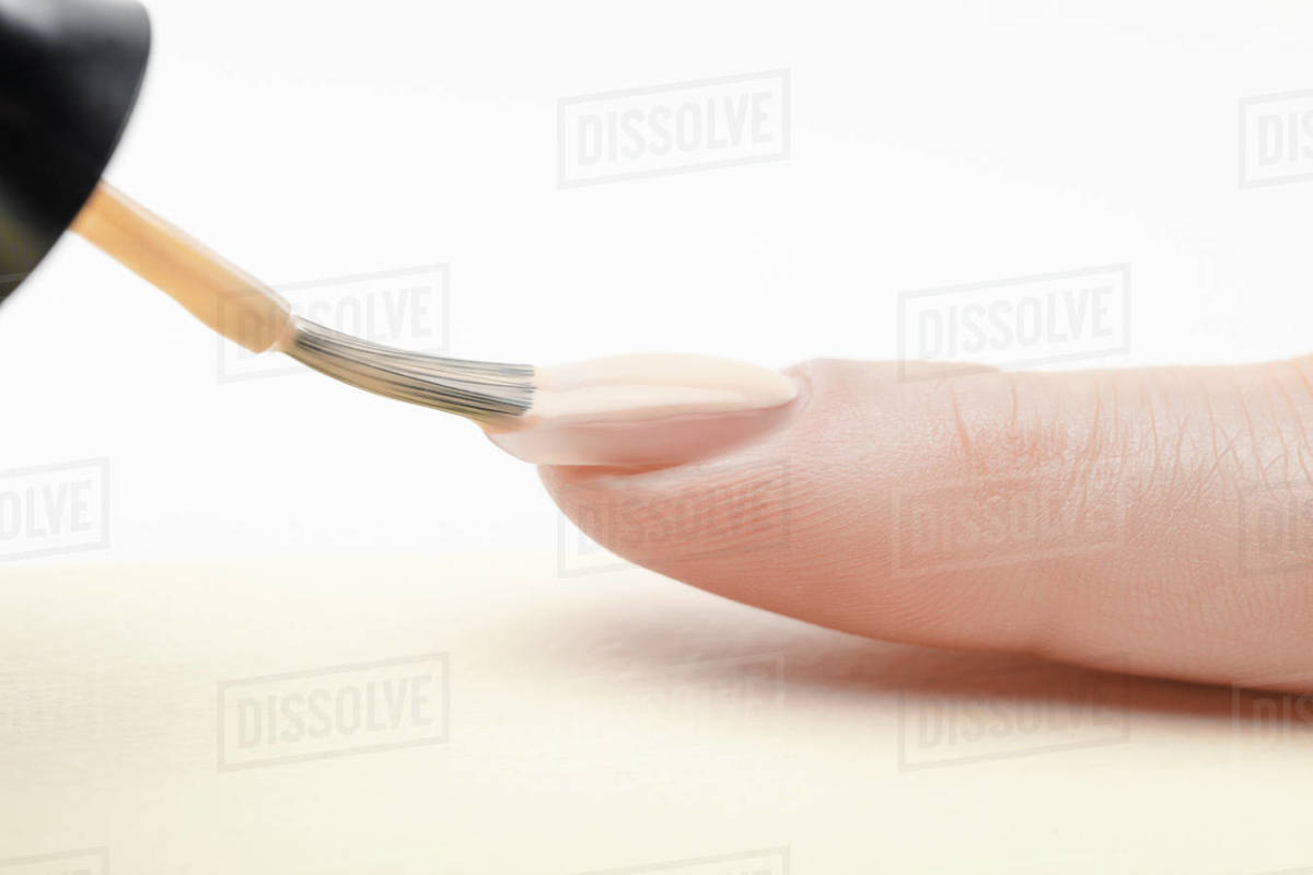 Ivory nail polish on fingernail of woman with wet brush on white ...