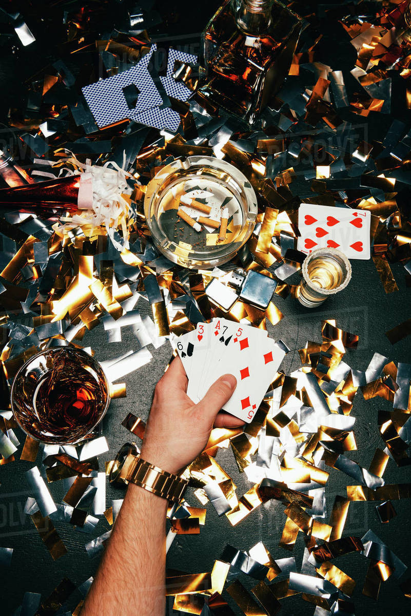 Cropped image of man with playing cards and alcohol sitting at table ...