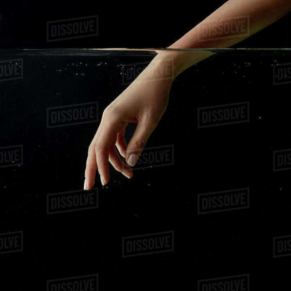 Partial view of girl putting hand into clear water isolated on black ...