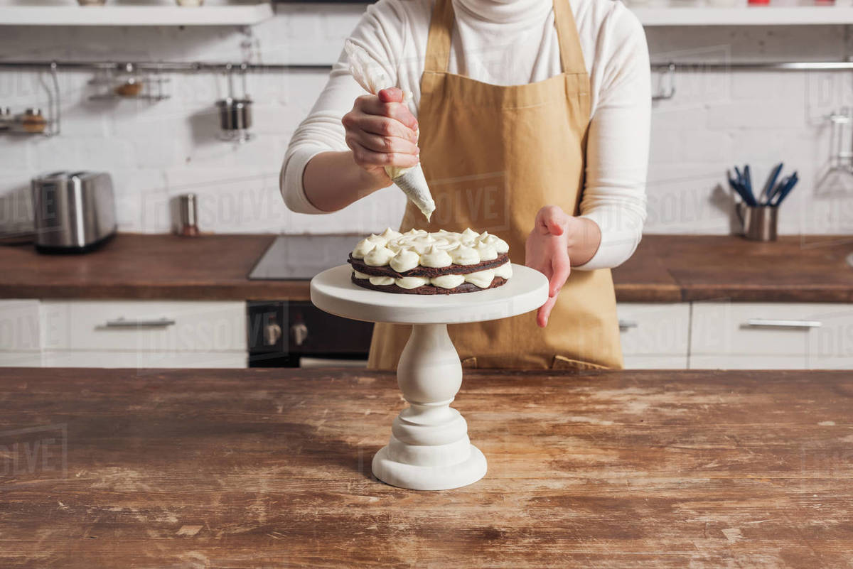 Cropped shot of woman in apron decorating gourmet sweet cake with cream ...
