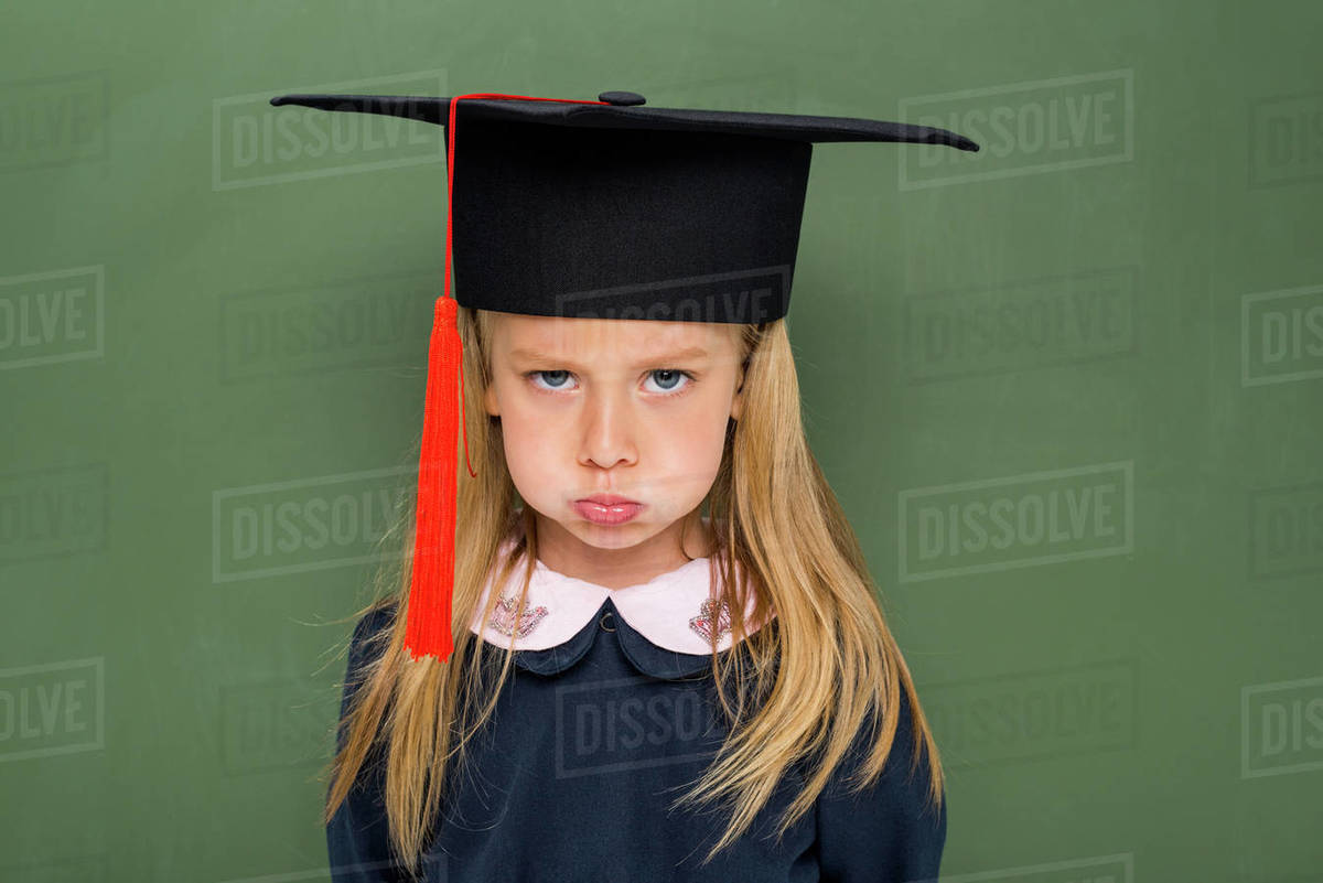Sad schoolgirl in graduation hat next to chalkboard - Royalty-free ...