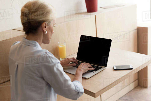 Back view of mature woman using laptop with blank screen in cafe ...