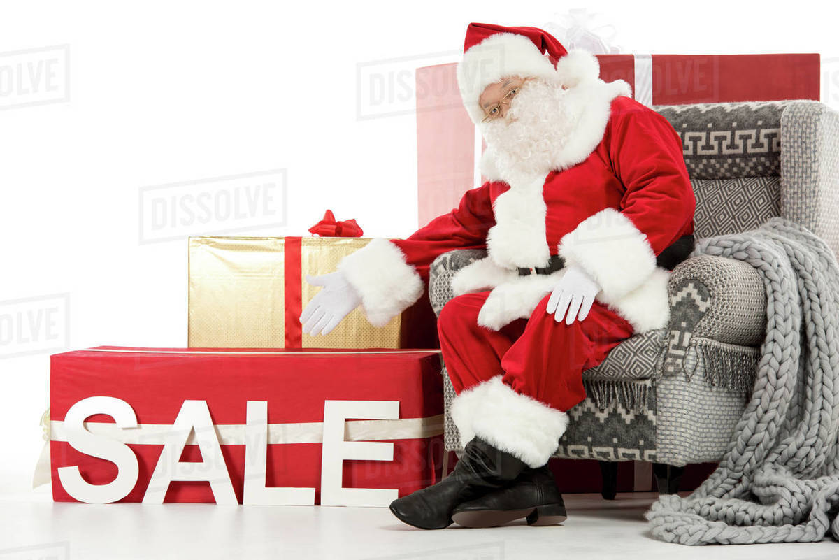 Santa Claus sitting on grey armchair and pointing on sale sign with ...
